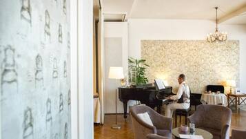 Um hall de hotel com um piano de cauda, assentos confortáveis e papel de parede estampado.