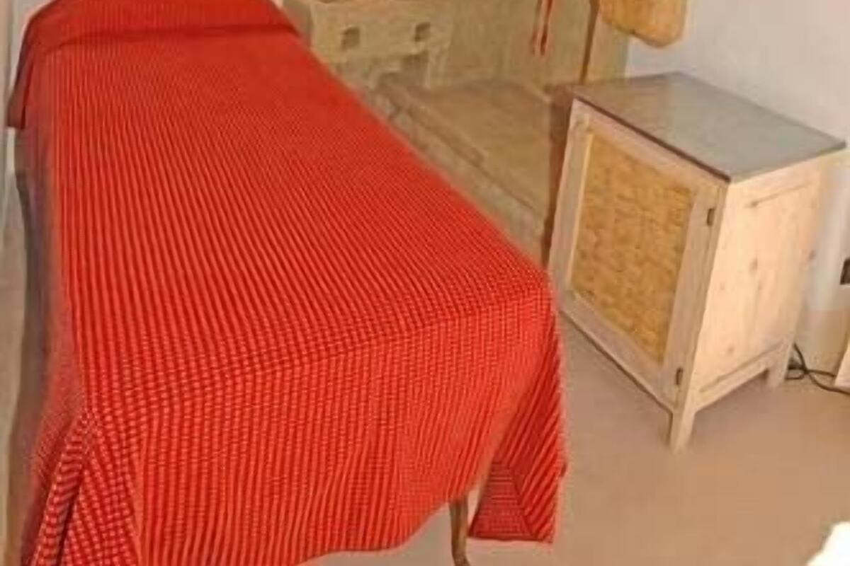 Quarto com cama, mesa pequena, televisão e painel na parede que lembra pedra.