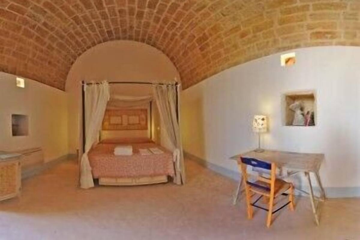 Quarto com cama de dossel, escrivaninha e uma cadeira.