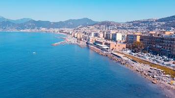 Paisagem costeira com um porto de iates, edifícios à beira-mar e montanhas ao fundo.