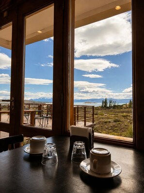 Mesa de jantar com chávenas e copos, com vista para uma paisagem deslumbrante com montanhas e um corpo de água.
