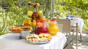 Uma mesa posta ao ar livre com uma variedade de frutas, uma torta e recipientes com suco.