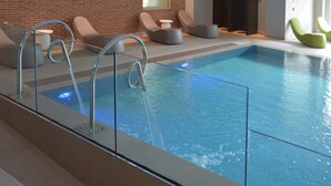 Uma piscina interna com espreguiçadeiras modernas e guarda-corpo de vidro.