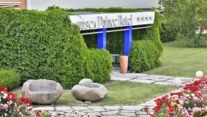Um caminho de jardim leva a um edifício com uma placa indicando 'Musca Palace Hotel'.