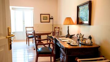 Uma área de refeições com mesa e cadeiras de madeira, uma luminária, um quadro na parede e um espaço para café com xícaras e chaleira.