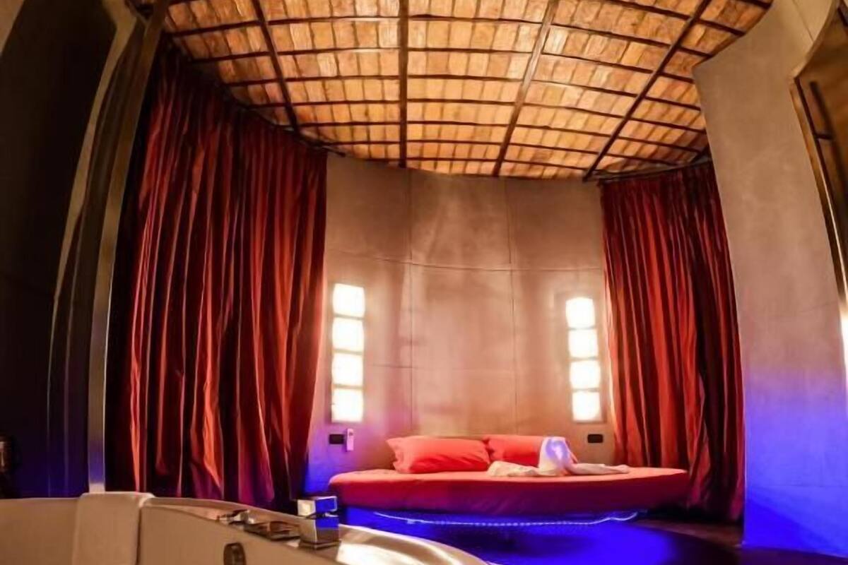 Um quarto de spa com uma banheira grande, cortinas vermelhas e um banco curvo.