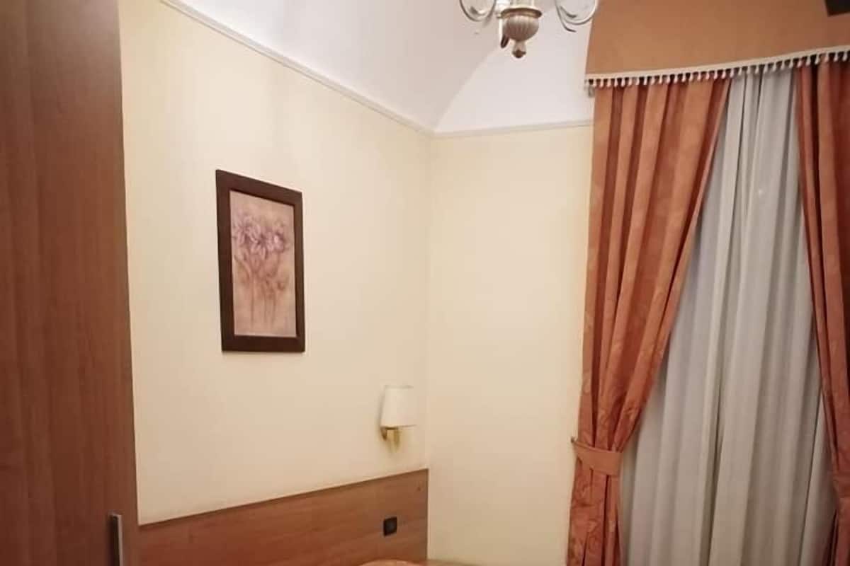 Quarto de hotel com cama, escrivaninha, cadeira, luminária e um quadro na parede.