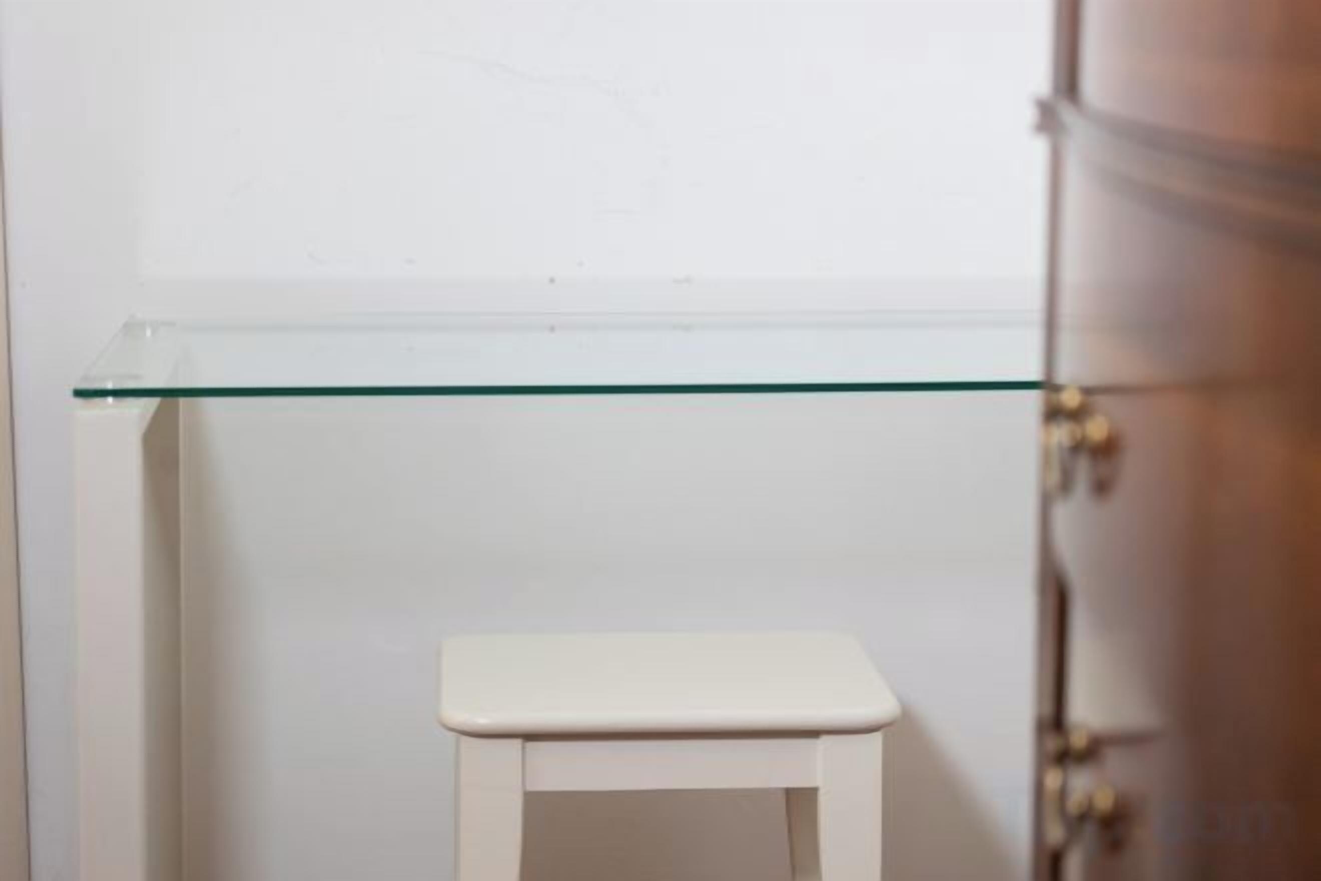 Um banquinho branco pequeno ao lado de uma prateleira de vidro.