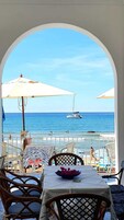 Um terraço à beira-mar com mesa, cadeiras e guarda-sóis, com vista para o oceano.