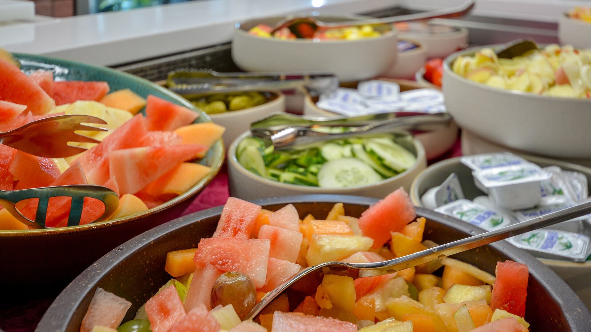 Buffet com diversos pratos, incluindo melancia, pepinos e outras frutas.