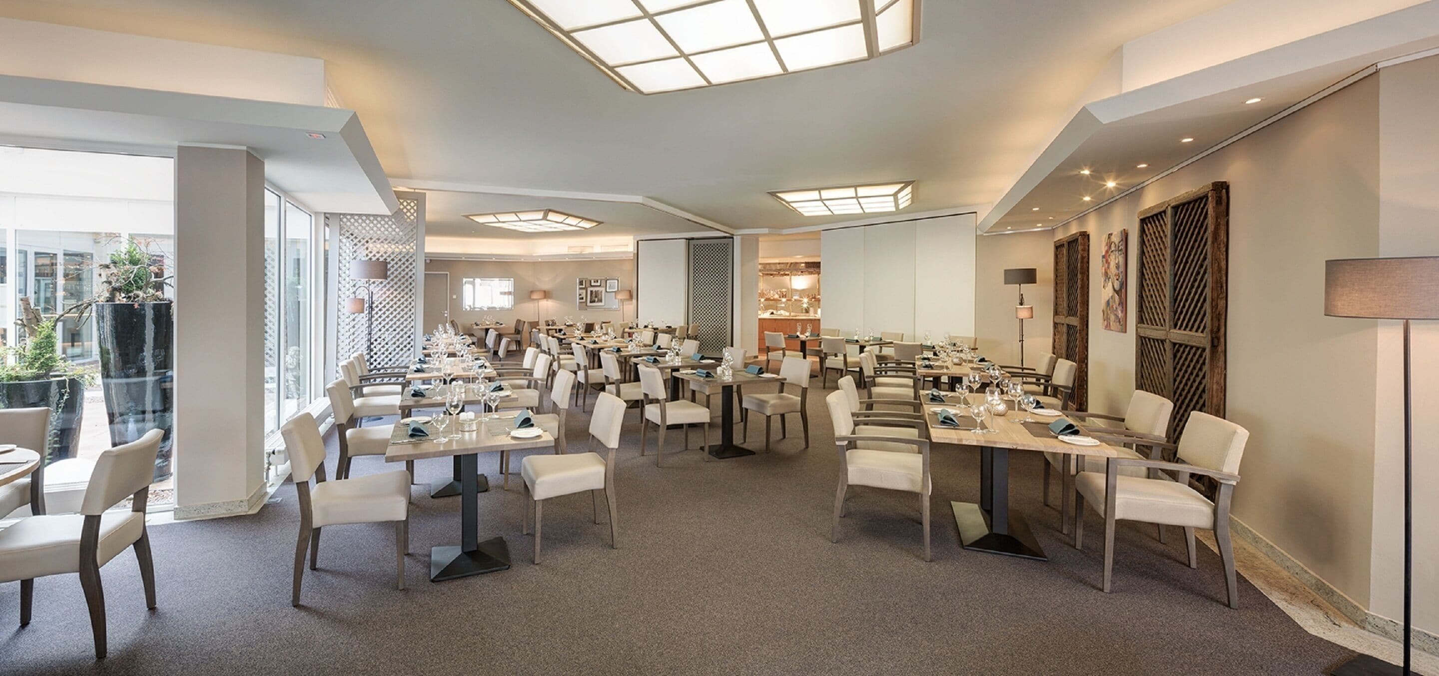 Uma sala de jantar ampla, com várias mesas e cadeiras, janelas grandes e design de interiores moderno.