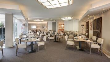 Uma sala de jantar ampla, com várias mesas e cadeiras, janelas grandes e design de interiores moderno.