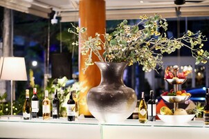 Uma área de bar com diversos frascos, um vaso grande com flores secas e uma exposição de frutas.