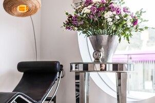 Quarto moderno com mesa de metal que suporta um vaso de flores, uma cadeira preta e um lustre.