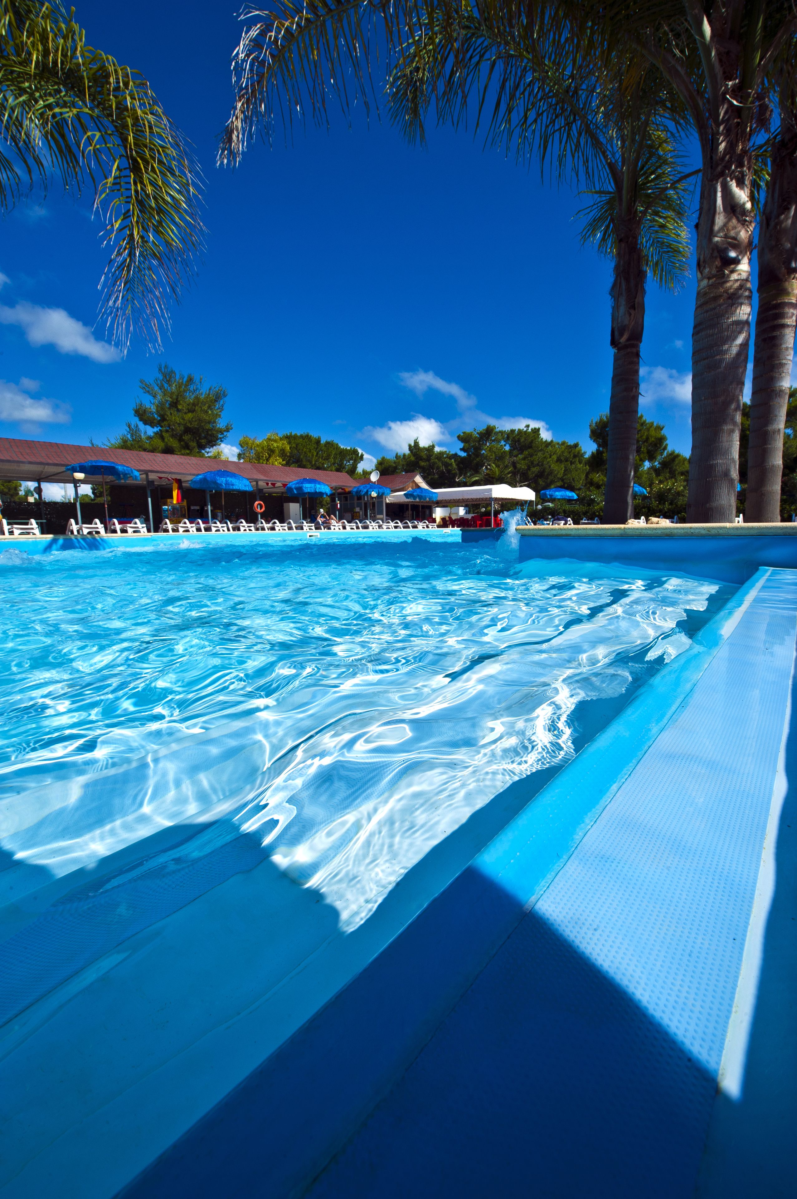 Piscina com água azul cristalina, cercada por palmeiras e guarda-sóis.