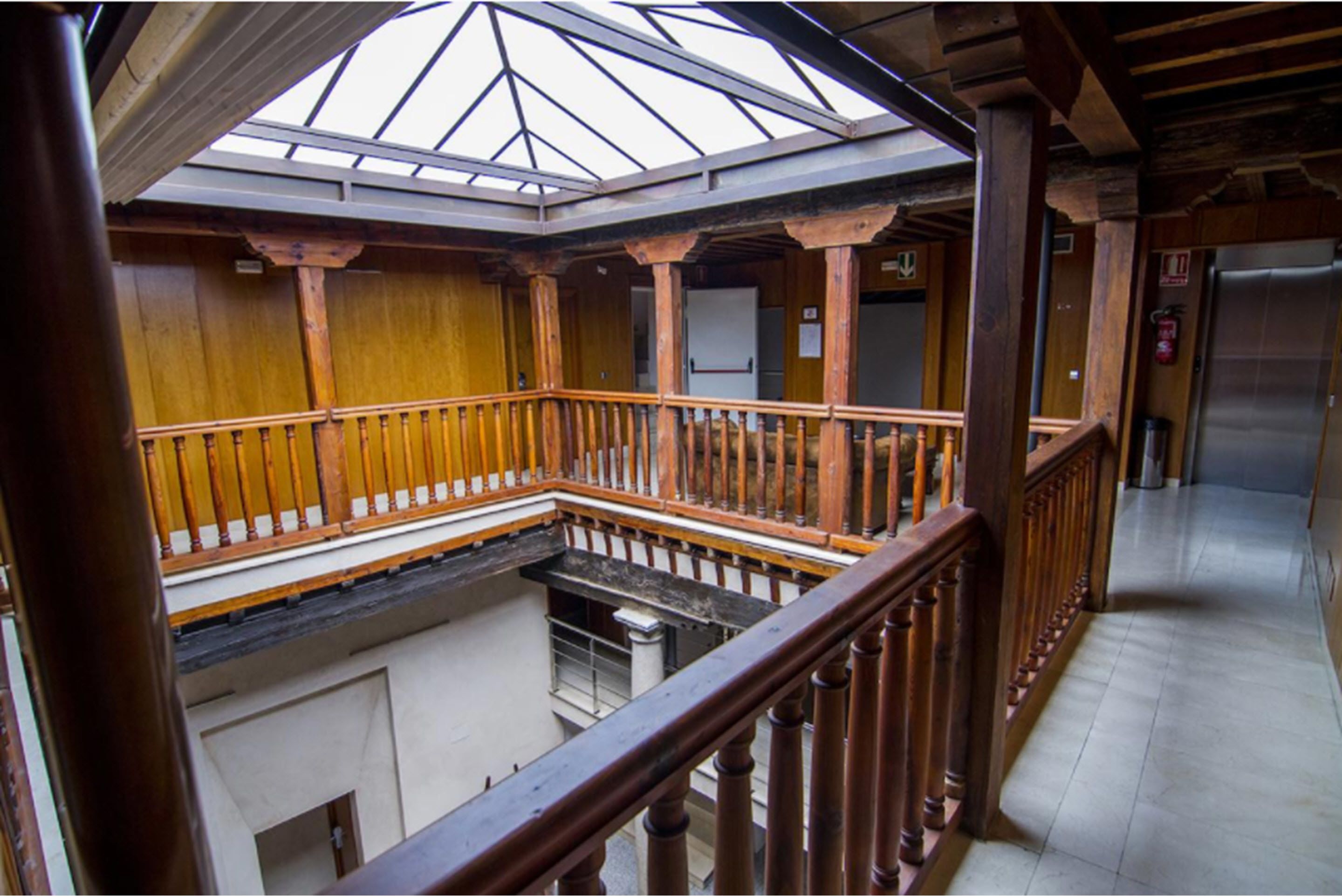Interior em madeira com teto de vidro, guarda-corpos de madeira e chão ladrilhado.