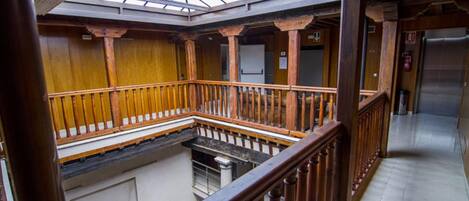 Interior em madeira com teto de vidro, guarda-corpos de madeira e chão ladrilhado.