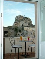 Varanda com duas cadeiras e uma mesa, com vista para um edifício histórico com uma cruz no topo.