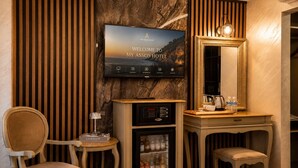 Quarto de hotel com televisão exibindo a mensagem de boas-vindas do hotel, um minibar, um espelho e um espaço de estar.