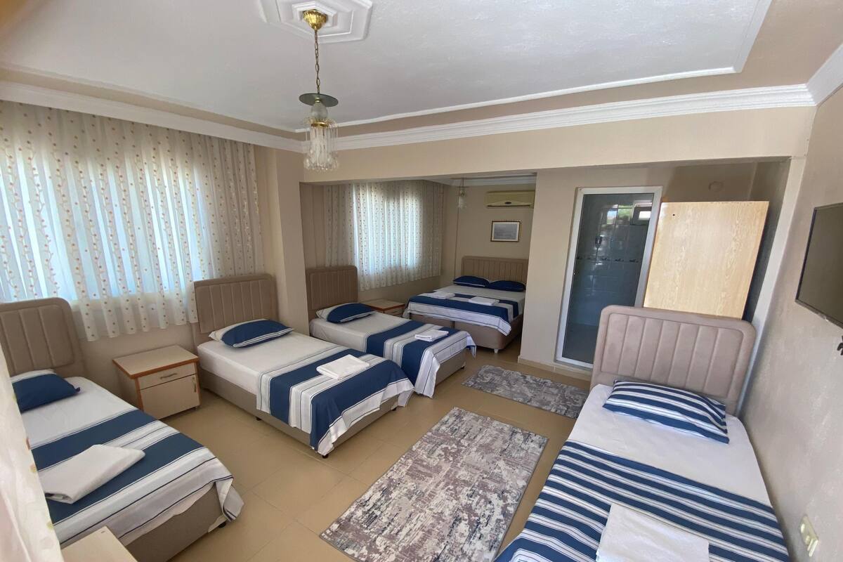 Quarto de hotel com três camas, uma escrivaninha, uma cadeira, um ventilador de teto e uma porta de vidro deslizante.