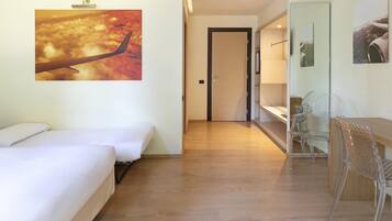 Quarto de hotel com cama, escrivaninha e uma cadeira. Há uma porta que dá para outro quarto.