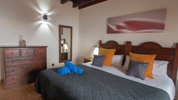 Cama bem arrumada com colcha escura, cabeceira de madeira e várias almofadas em cores diferentes.