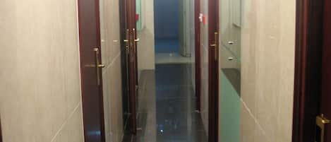 Um corredor com portas de ambos os lados, chão ladrilhado e teto com iluminação.
