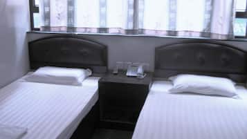 Quarto de hotel com duas camas de solteiro, uma mesinha com telefone e uma janela com cortinas.
