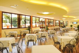 Uma ampla área de refeições interna com várias mesas e cadeiras, janelas grandes com vista para o exterior e um design de teto moderno.