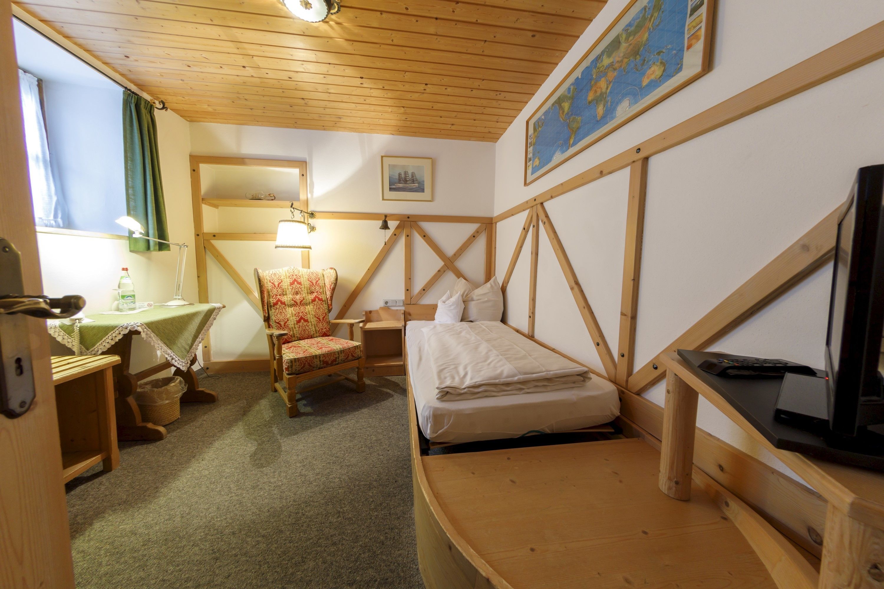 Quarto com cama, cadeira, mesa pequena, televisão e mapa na parede.