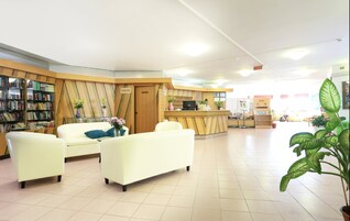 Uma área de recepção com balcão, um sofá branco e uma estante.