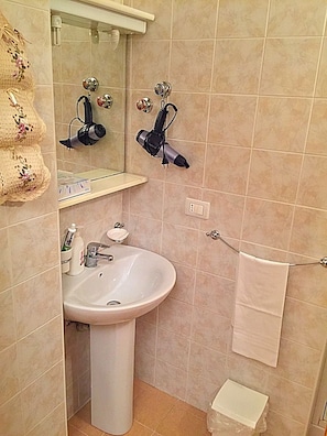 Casa de banho com lavatório, espelho, porta-toalhas e um pequeno cesto de lixo.