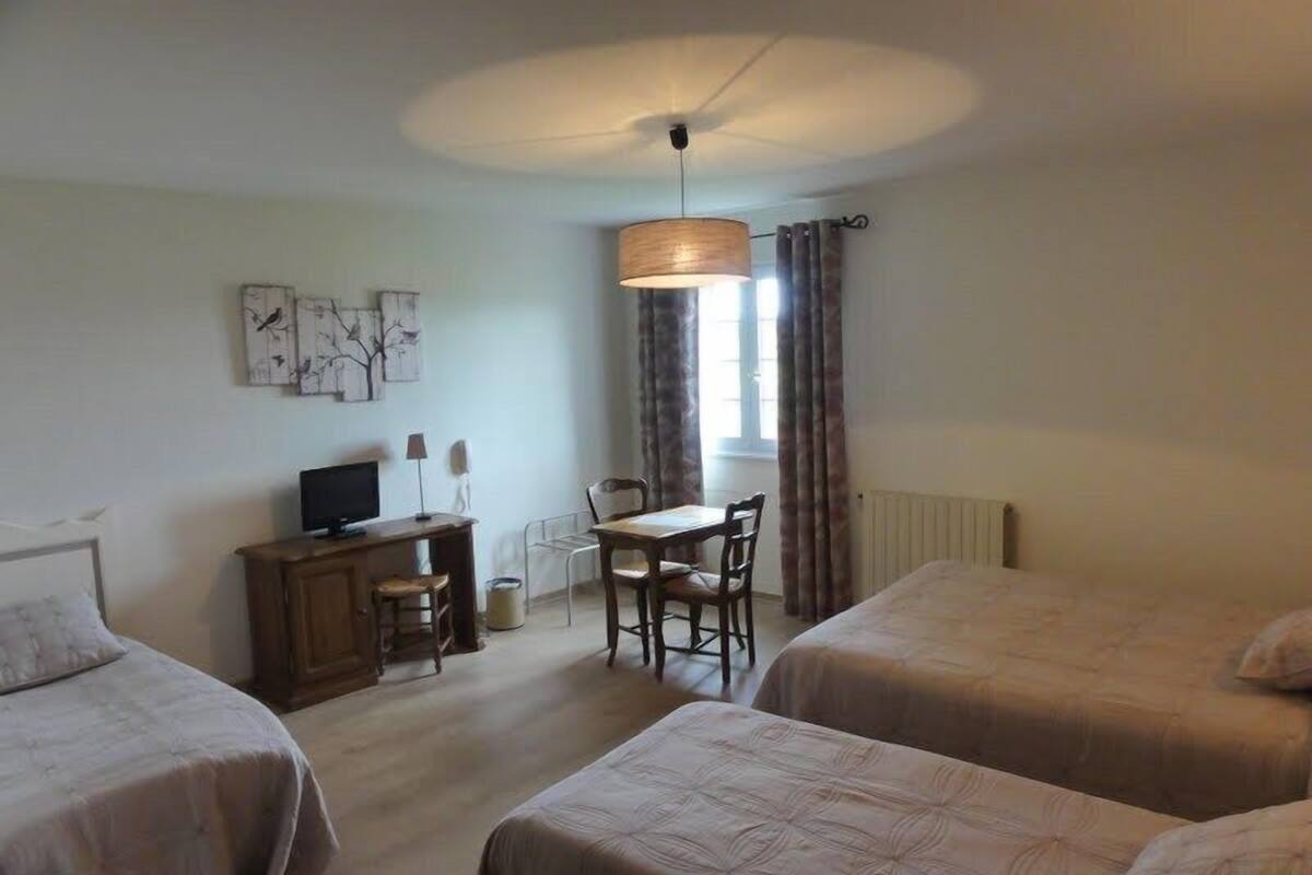Quarto de hotel com duas camas, uma escrivaninha com computador, uma cadeira e uma janela com cortinas.