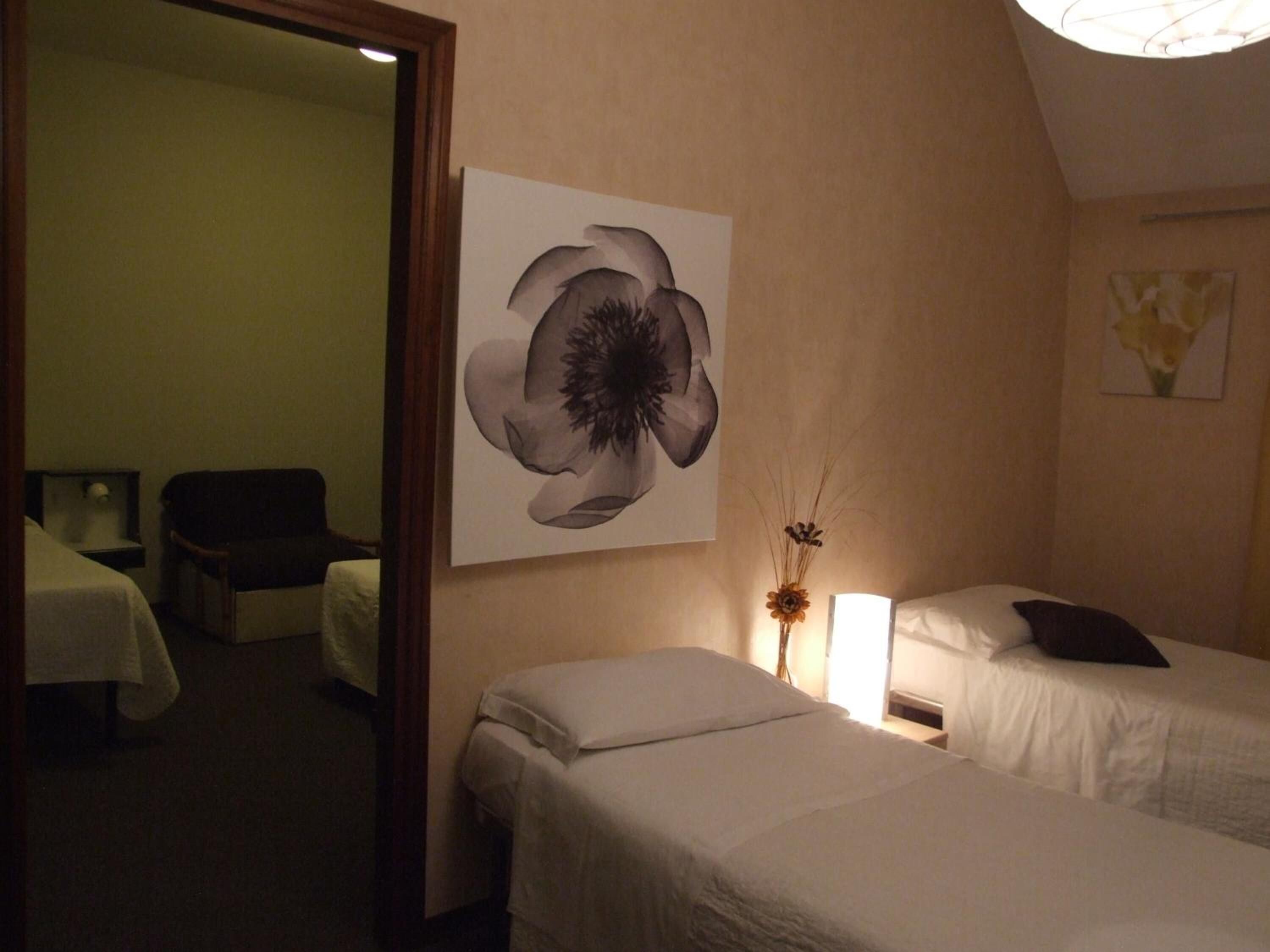 Quarto de hotel com duas camas, um espelho, um quadro e um vaso com flores secas.