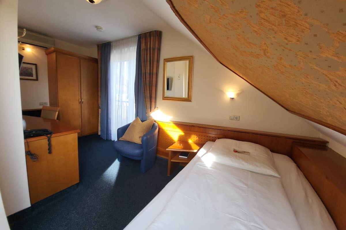 Quarto de hotel com cama, escrivaninha, cadeira, guarda-roupa e espelho.