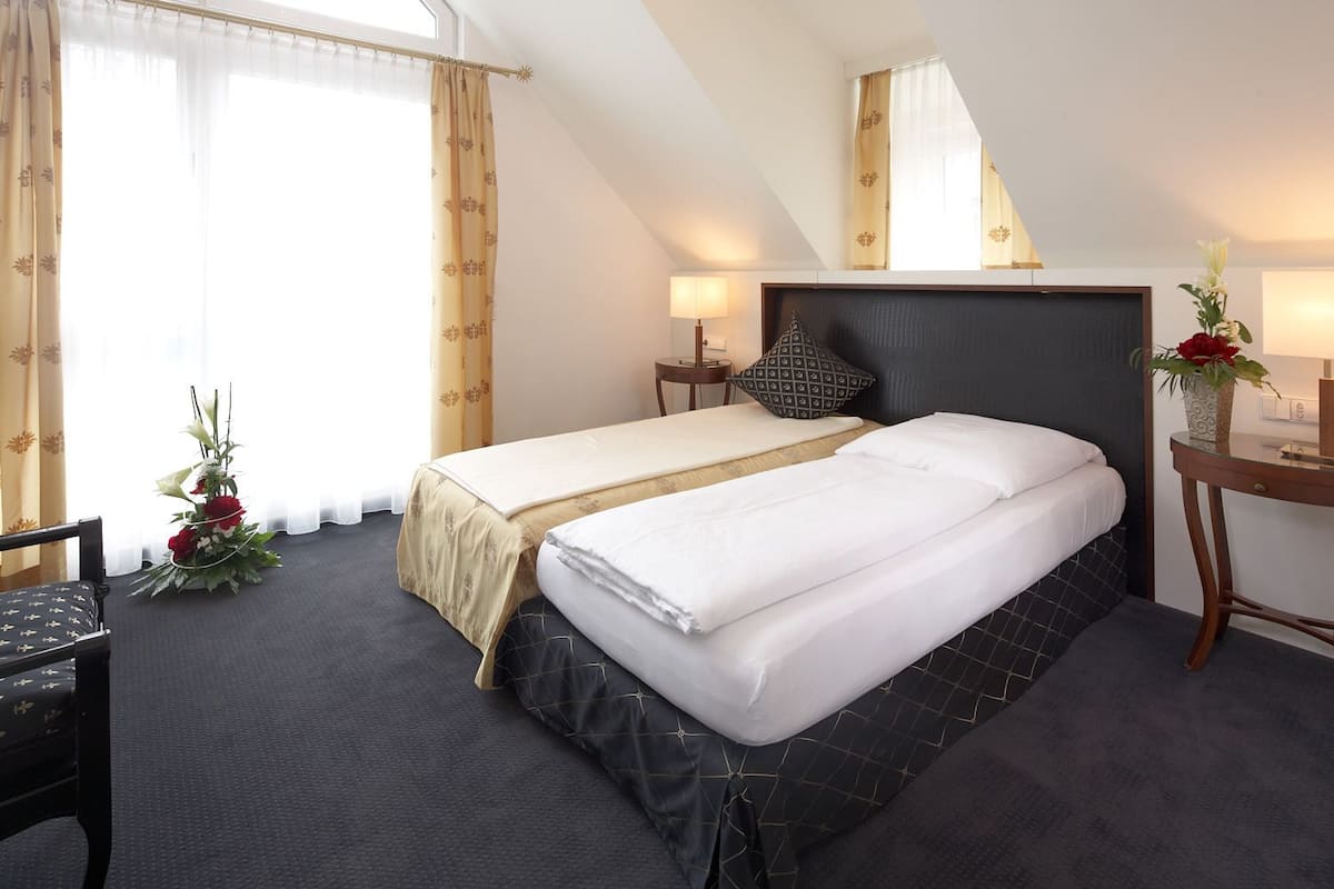 Quarto de hotel com cama, mesas de cabeceira, uma cadeira e uma escrivaninha com luminária.