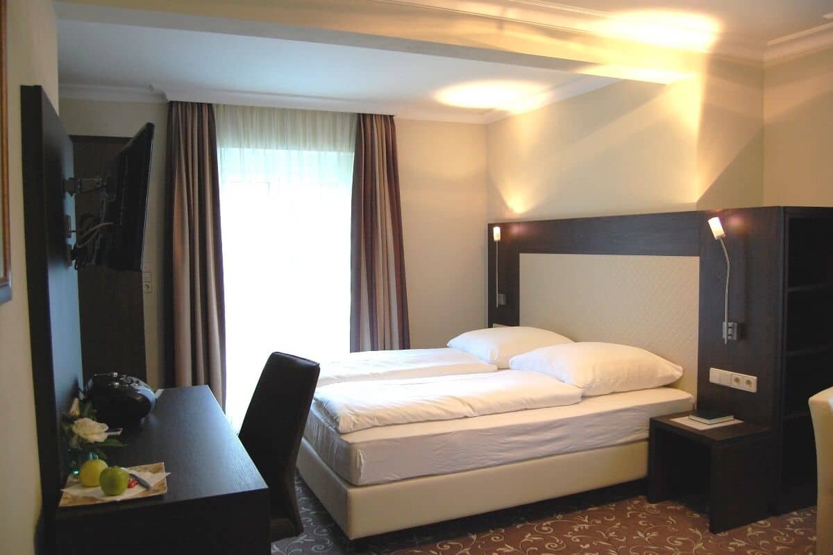 Quarto de hotel com duas camas, uma escrivaninha com cadeira, televisão e guarda-roupa.