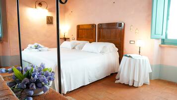 Quarto de hotel com cama de casal, uma pequena mesa com abajur e um vaso de flores.