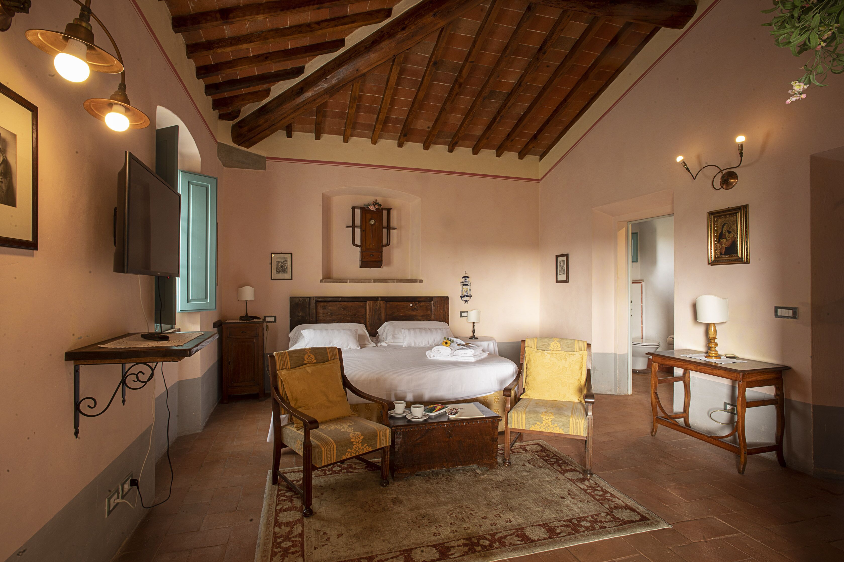 Um quarto com cama, duas cadeiras, mesa de cabeceira e teto de madeira.