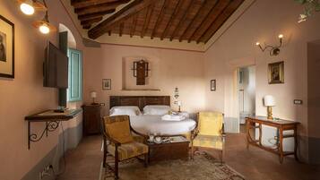 Um quarto com cama, duas cadeiras, mesa de cabeceira e teto de madeira.