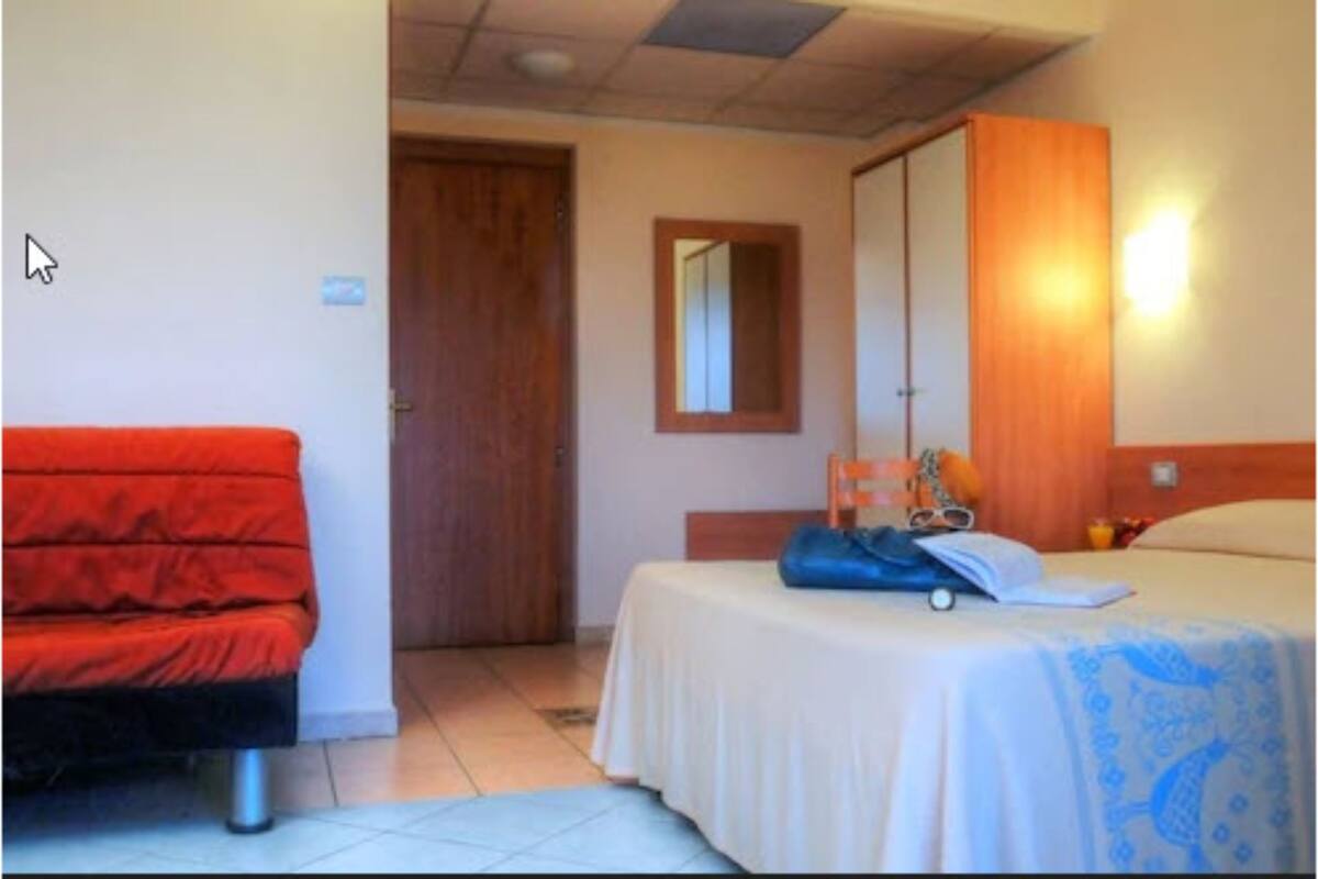 Quarto de hotel com cama, cadeira, guarda-roupa e espelho.