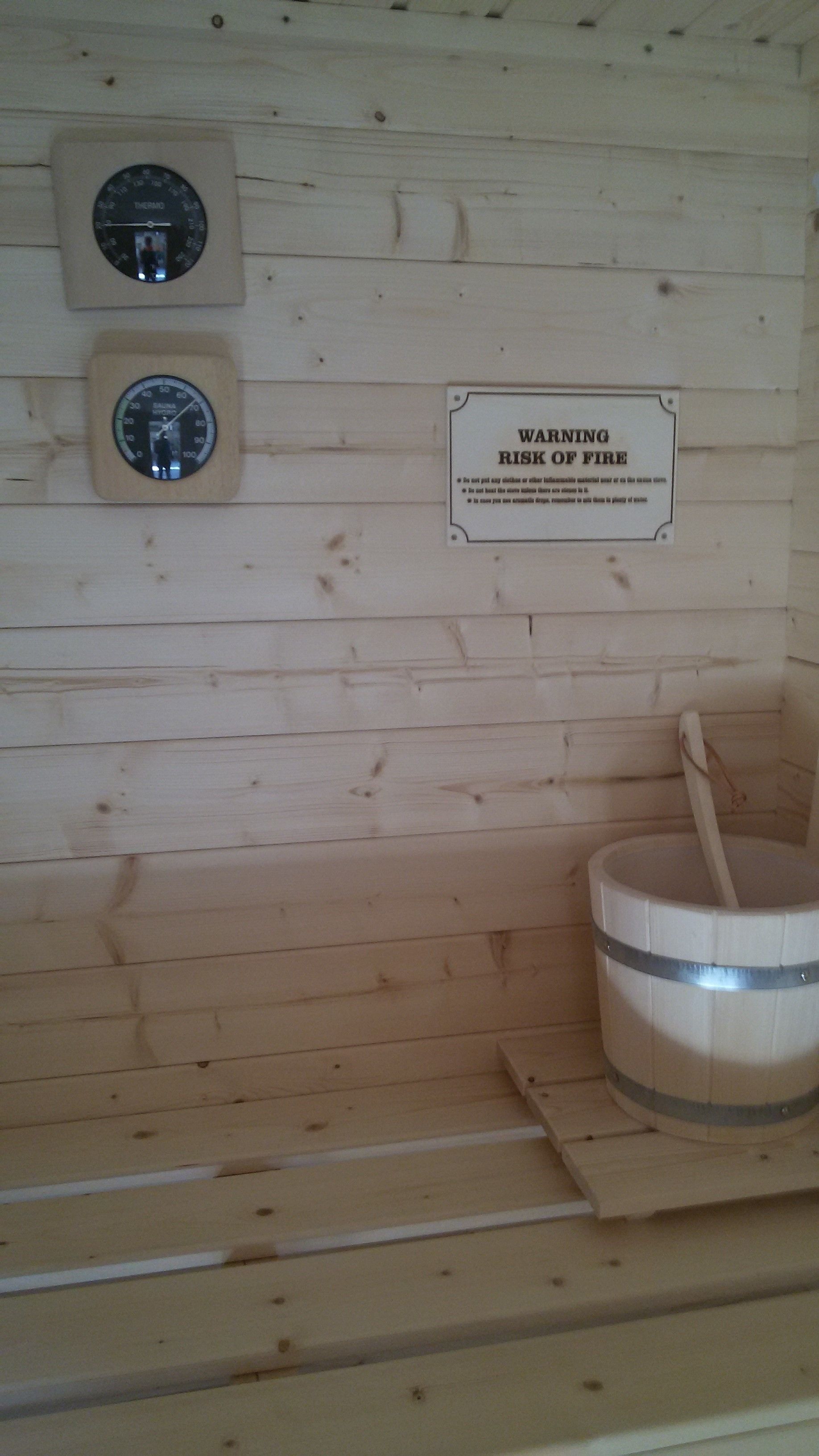 Uma sauna com interior de madeira, um termômetro e um aviso sobre risco de incêndio.