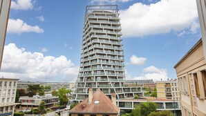 Um edifício moderno de muitos andares com várias varandas, cercado por outros edifícios e áreas verdes.