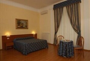 Um quarto com cama, uma mesa com cadeiras, um quadro na parede e cortinas.