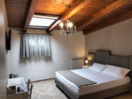 Quarto com cama, escrivaninha, cadeira, lustre e janela com cortinas.