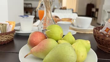 Uma mesa de jantar com um prato de frutas, um copo de suco de laranja e um vaso com plantas secas.