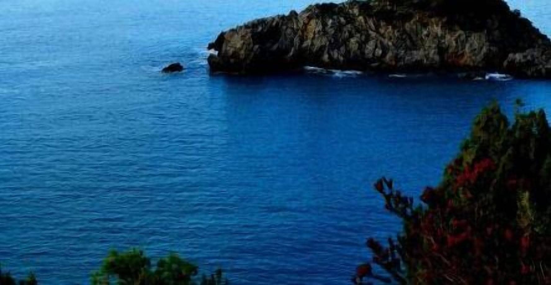 Paisagem costeira com um afloramento rochoso e mar calmo.