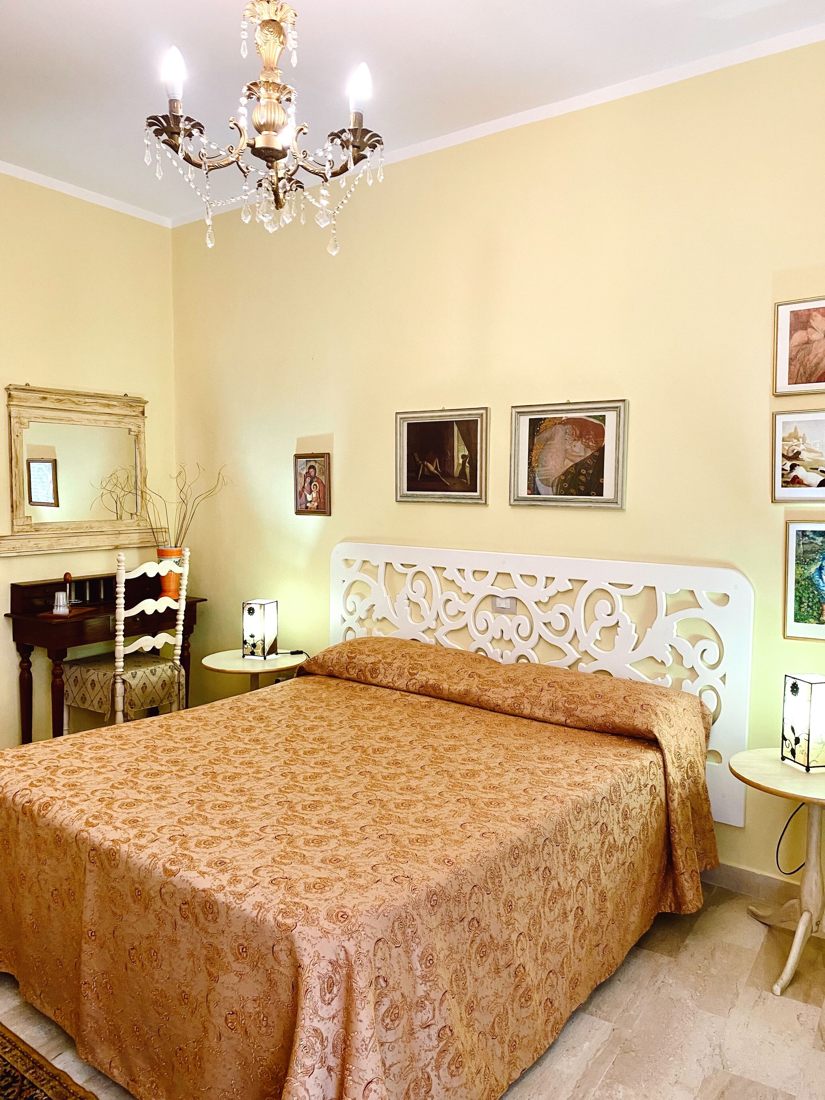 Quarto com cama grande, lustre, espelho e quadros nas paredes.
