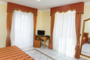 Quarto de hotel com cama, secretária e computador, e cortinas.