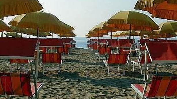 Uma praia com fileiras de guarda-sóis vermelhos e amarelos e cadeiras.